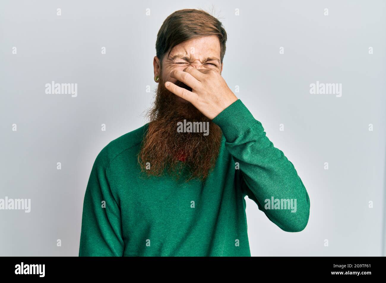 Redhead man with long beard wearing casual clothes smelling something ...