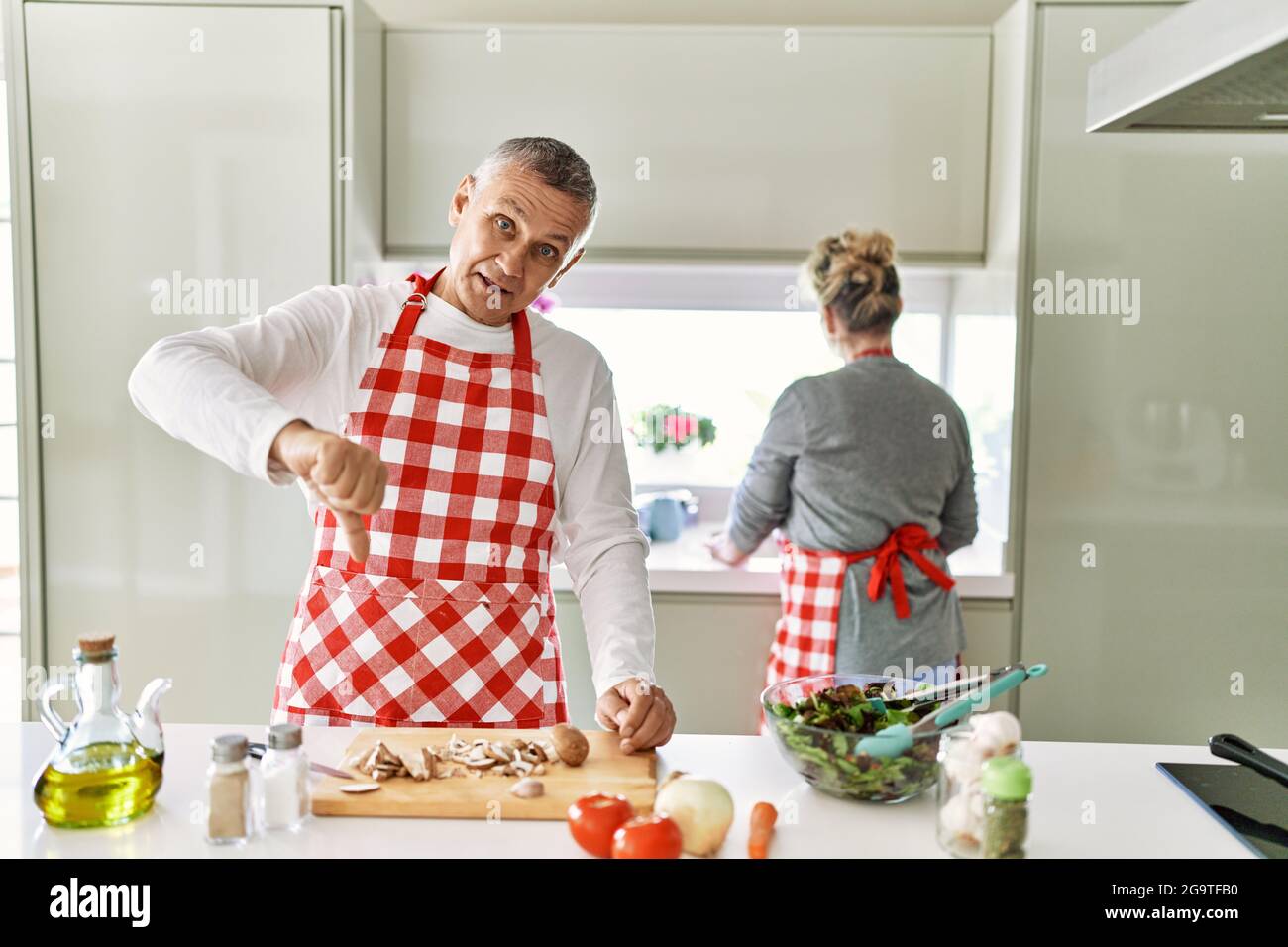 Middle age caucasian couple cooking healthy salad with angry face ...