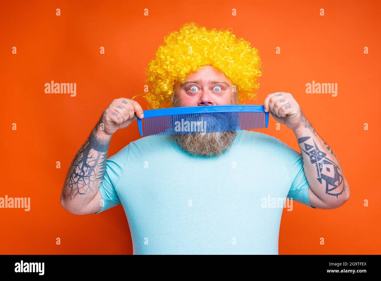 Fat amazed man with beard, tattoos and sunglasses combs himself with a ...