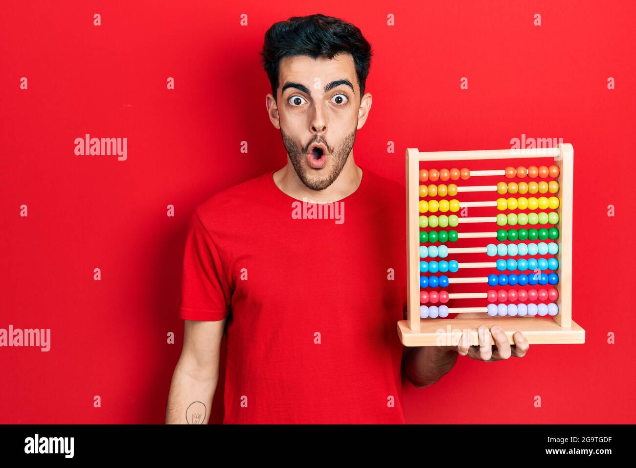 Young hispanic man holding traditional abacus scared and amazed with ...