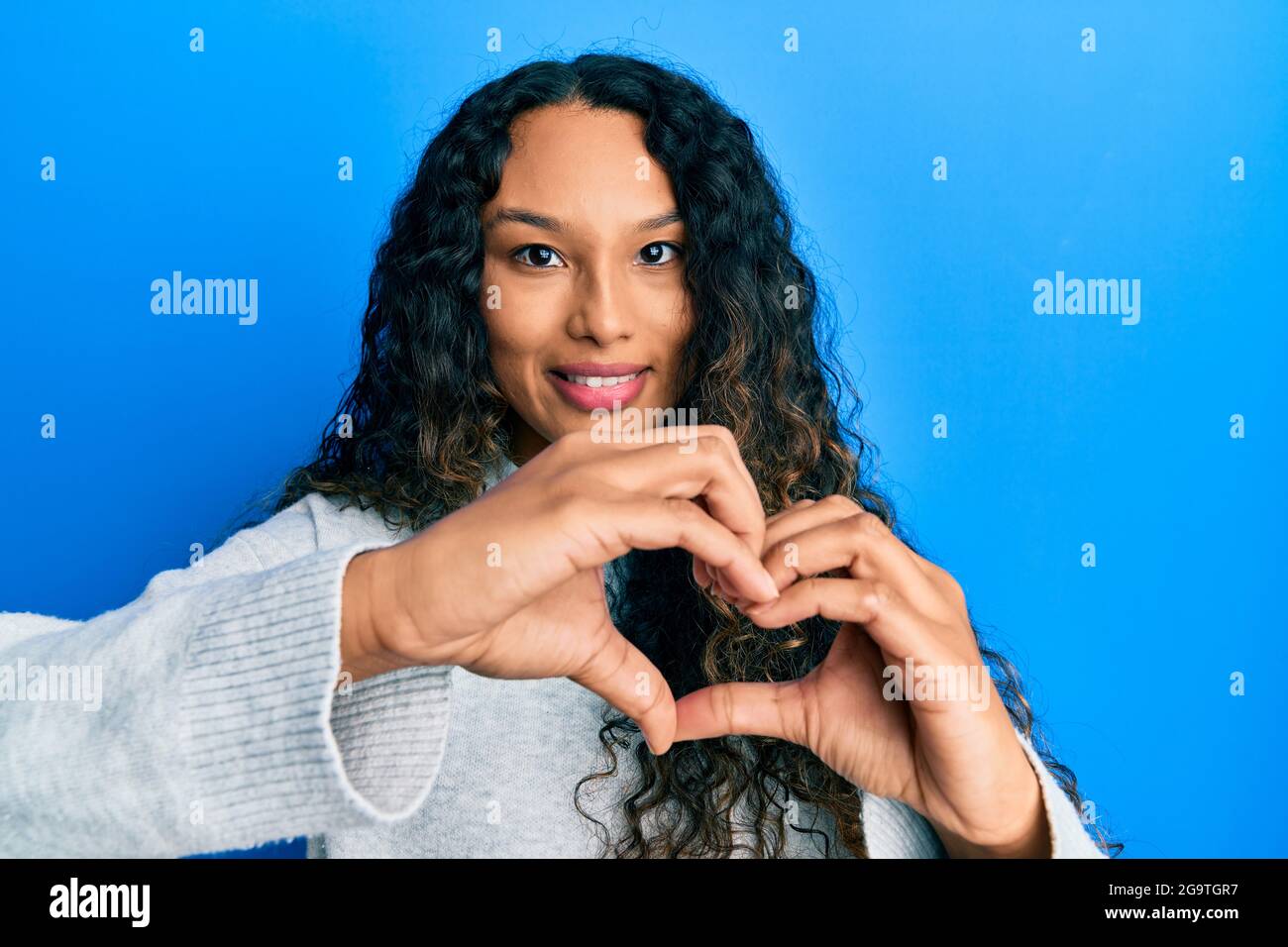 Young latin woman wearing casual clothes smiling in love doing heart ...