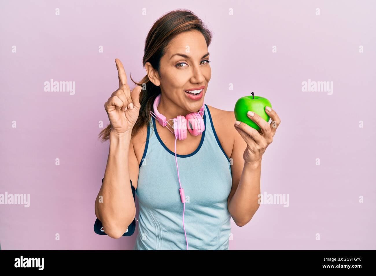 Young latin woman wearing gym clothes, using headphones and eating ...