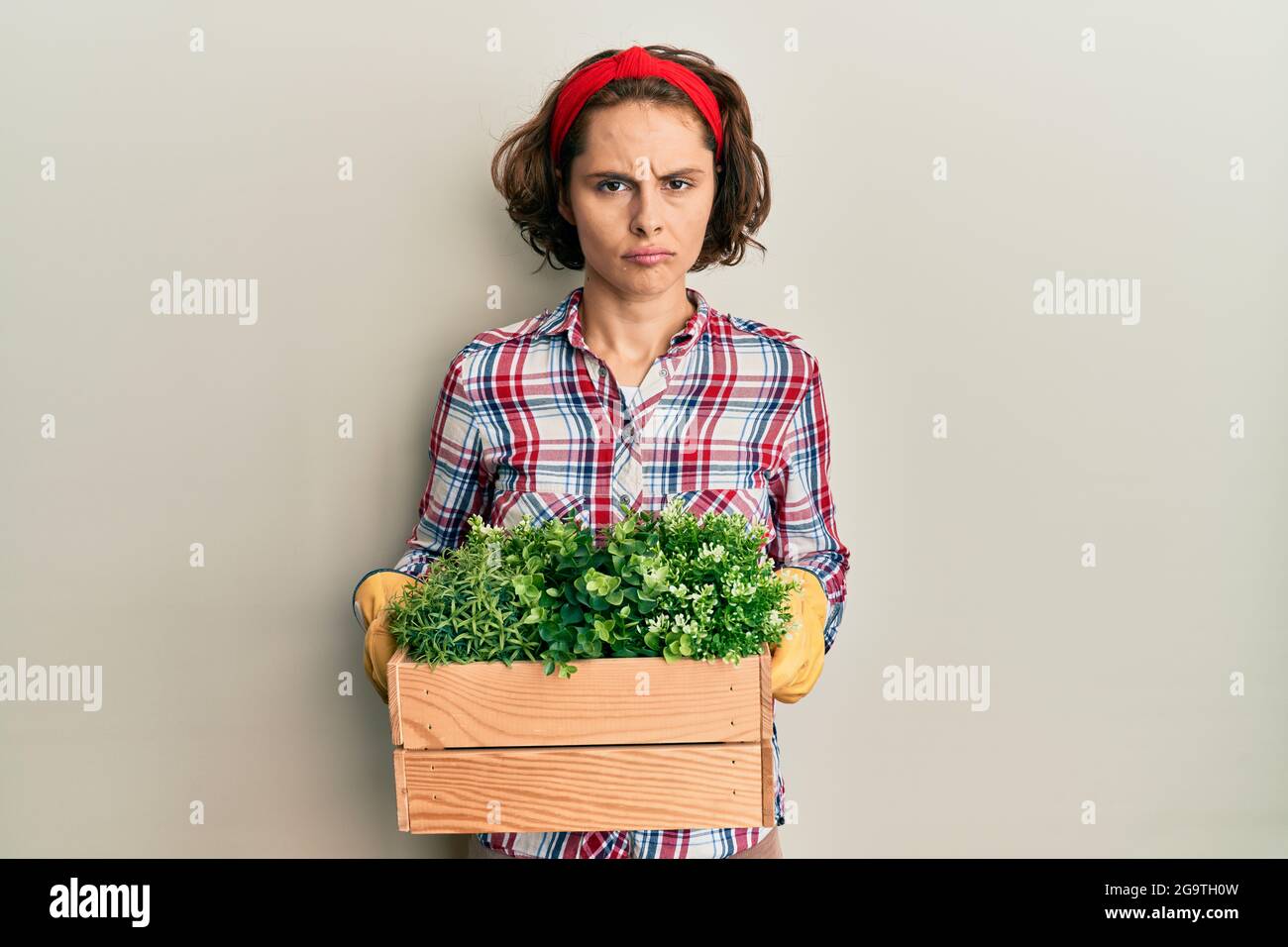 Young brunette woman wearing gardener clothes holding wooden plant pot ...