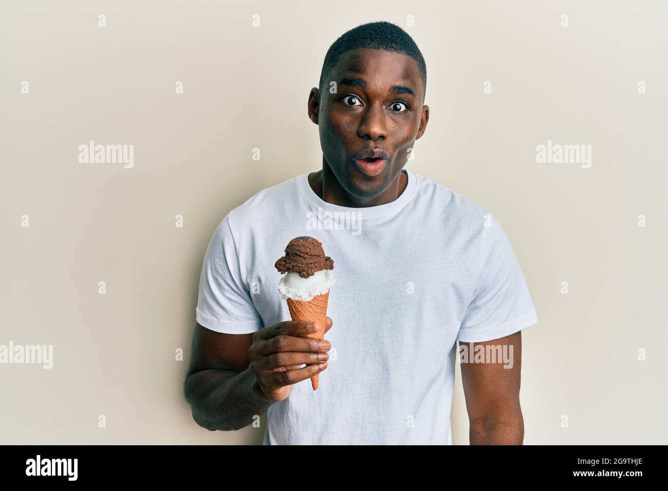 Young african american man holding ice cream scared and amazed with ...