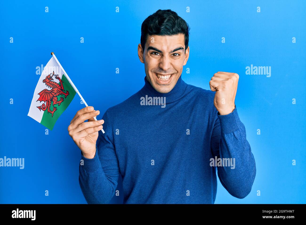 Handsome hispanic man holding wales flag screaming proud, celebrating ...