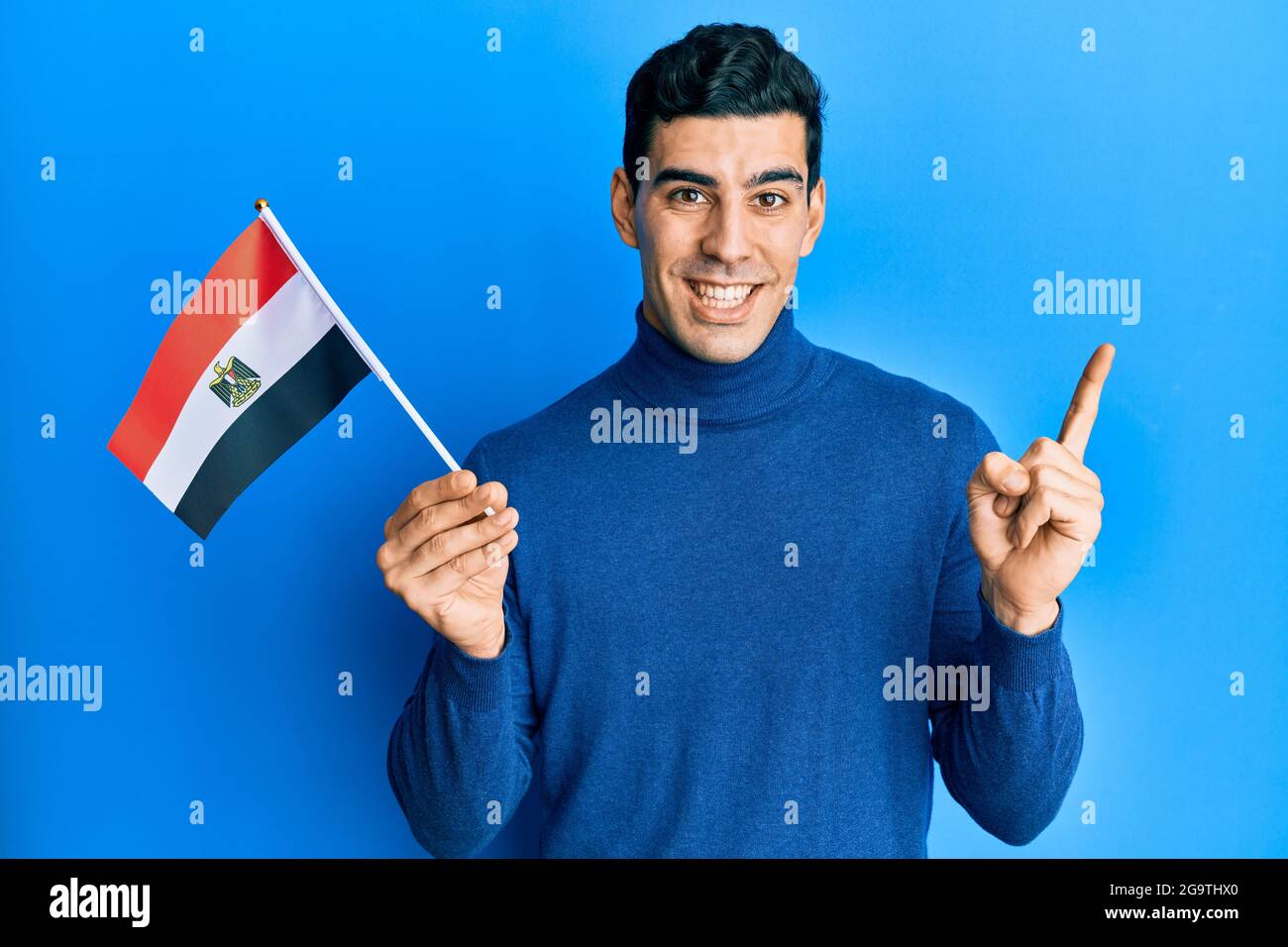 Handsome hispanic man holding egypt flag smiling happy pointing with ...