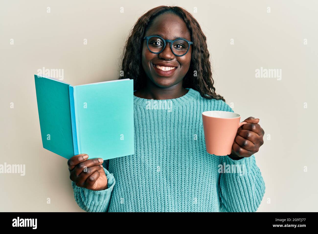 African young woman reading a book and drinking a cup of coffee smiling ...