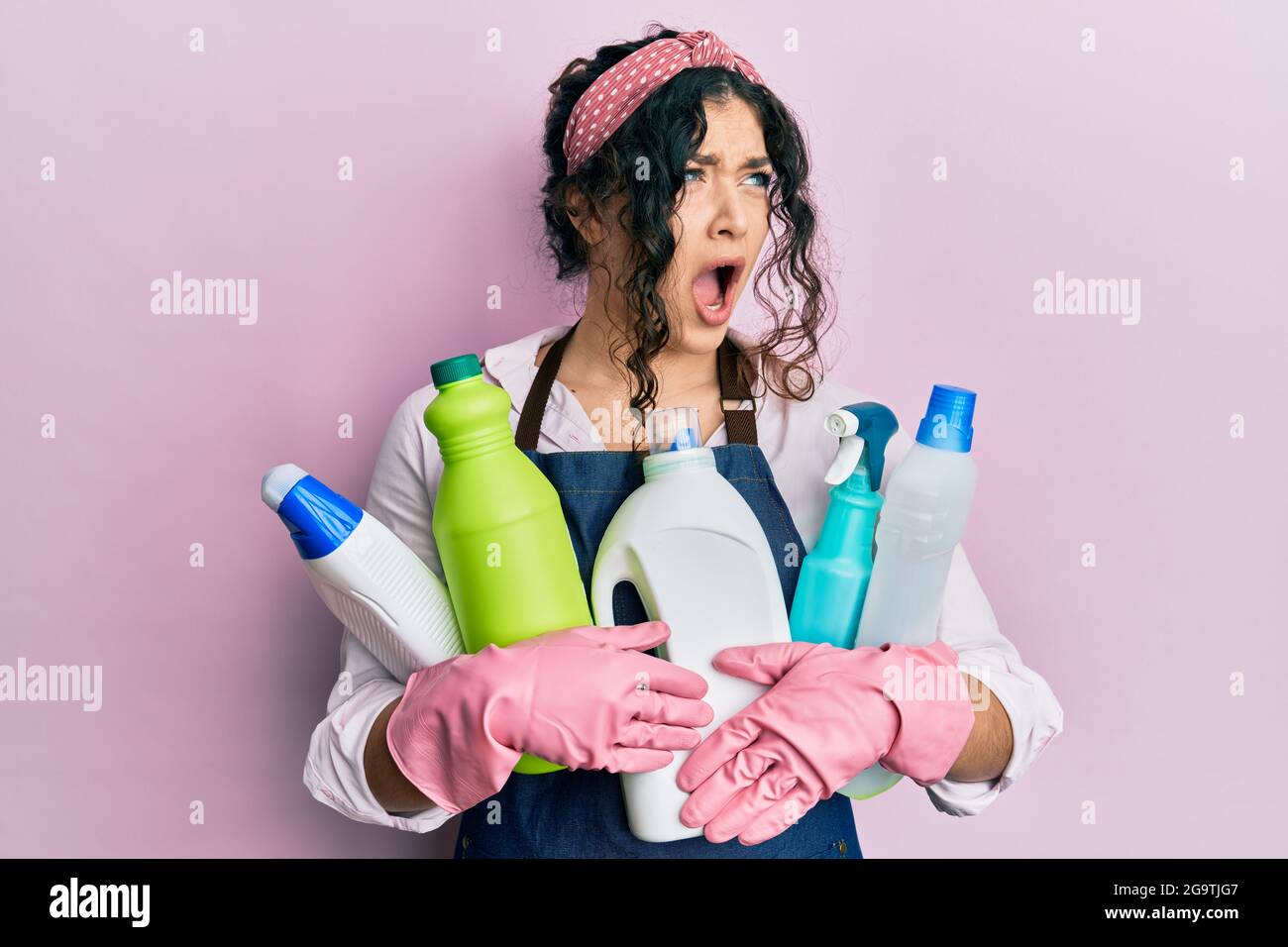 Young brunette woman with curly hair wearing cleaner apron holding ...