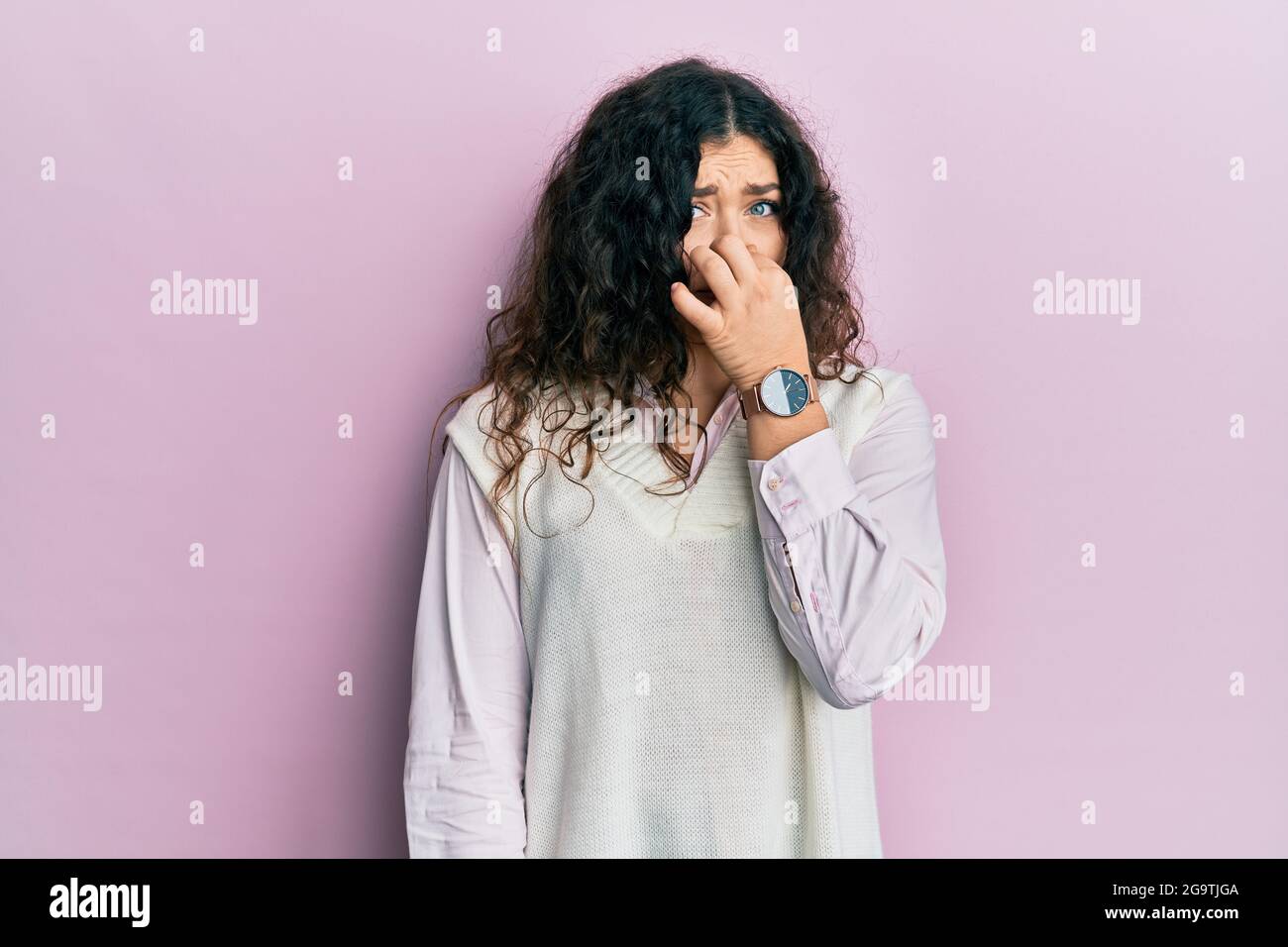 Young brunette woman with curly hair wearing casual clothes smelling ...