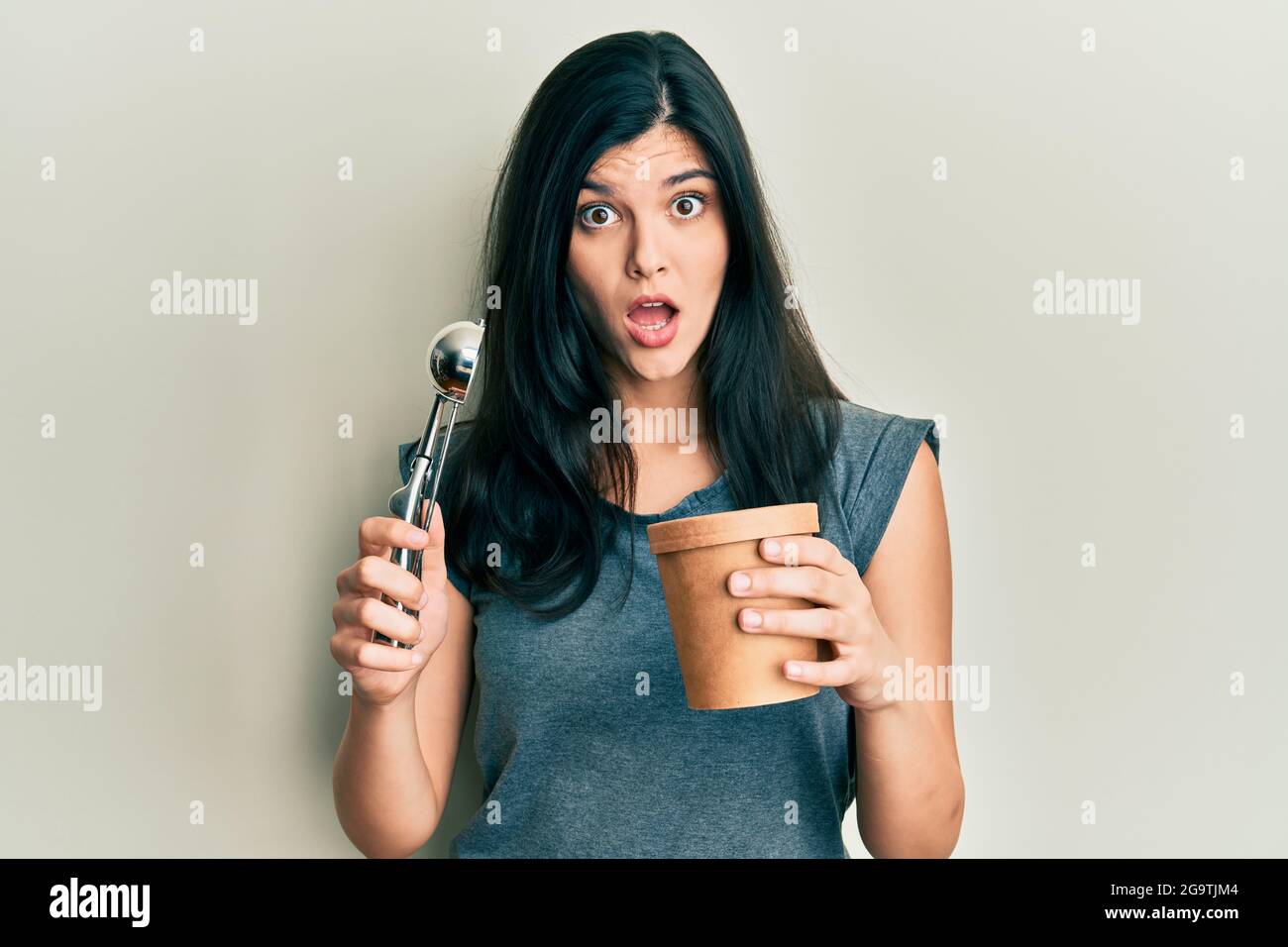 Young hispanic woman holding ice cream in shock face, looking skeptical ...