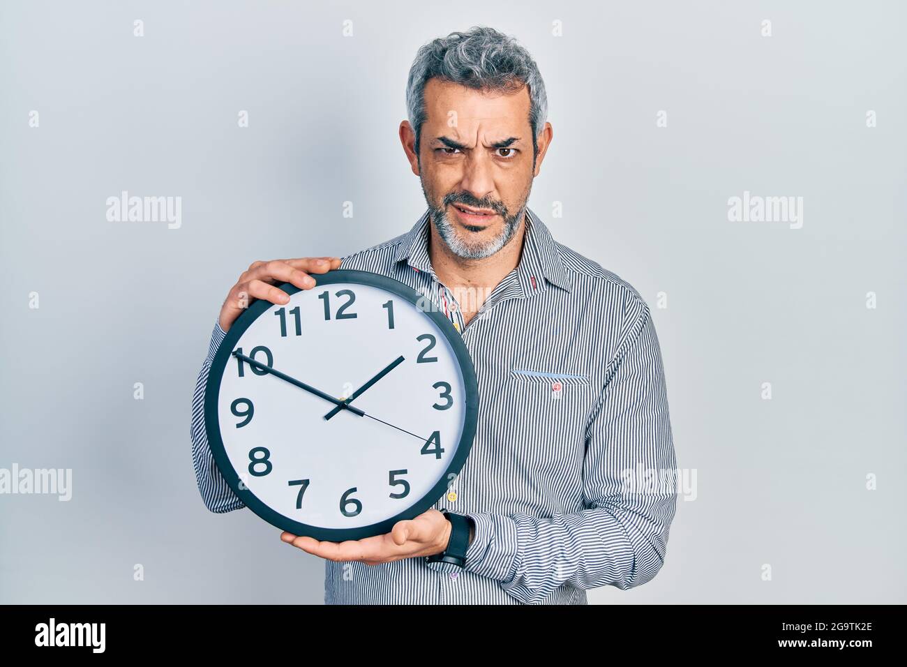 Handsome middle age man with grey hair holding big clock clueless and ...