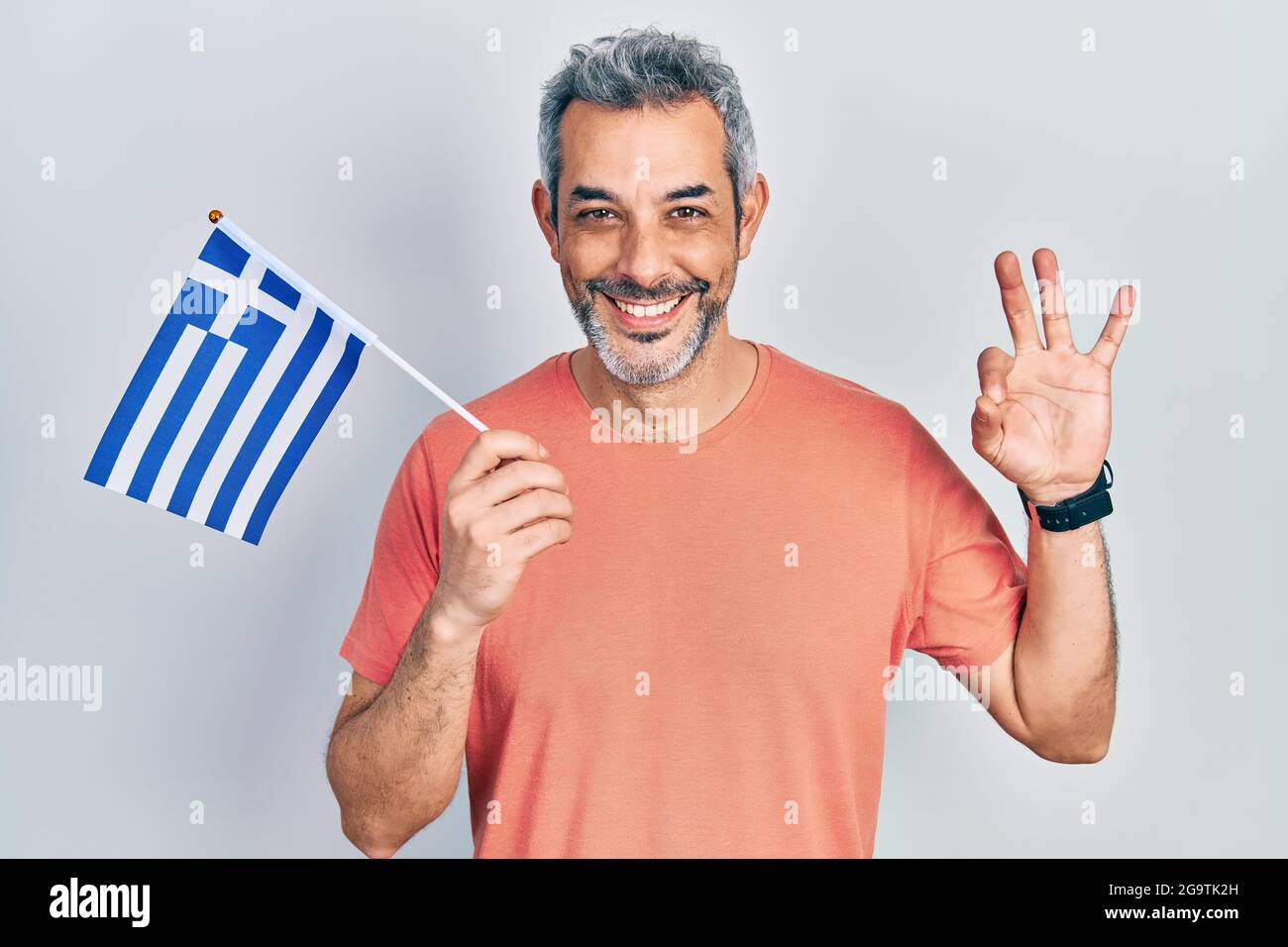 Handsome middle age man with grey hair holding greece flag doing ok ...