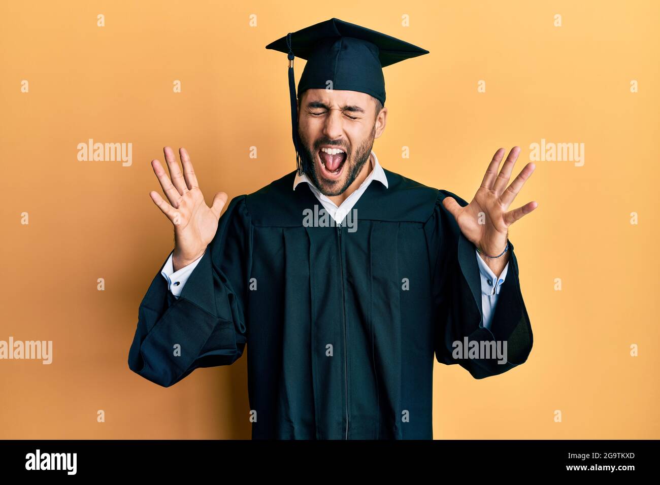 Young hispanic man wearing graduation cap and ceremony robe celebrating ...