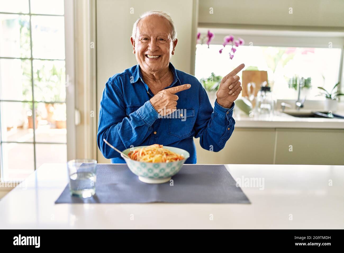 Senior man with grey hair eating pasta spaghetti at home smiling and ...