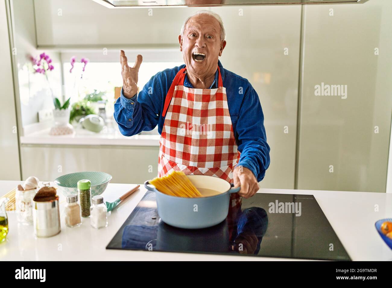 Senior man with grey hair cooking spaghetti at home kitchen celebrating ...