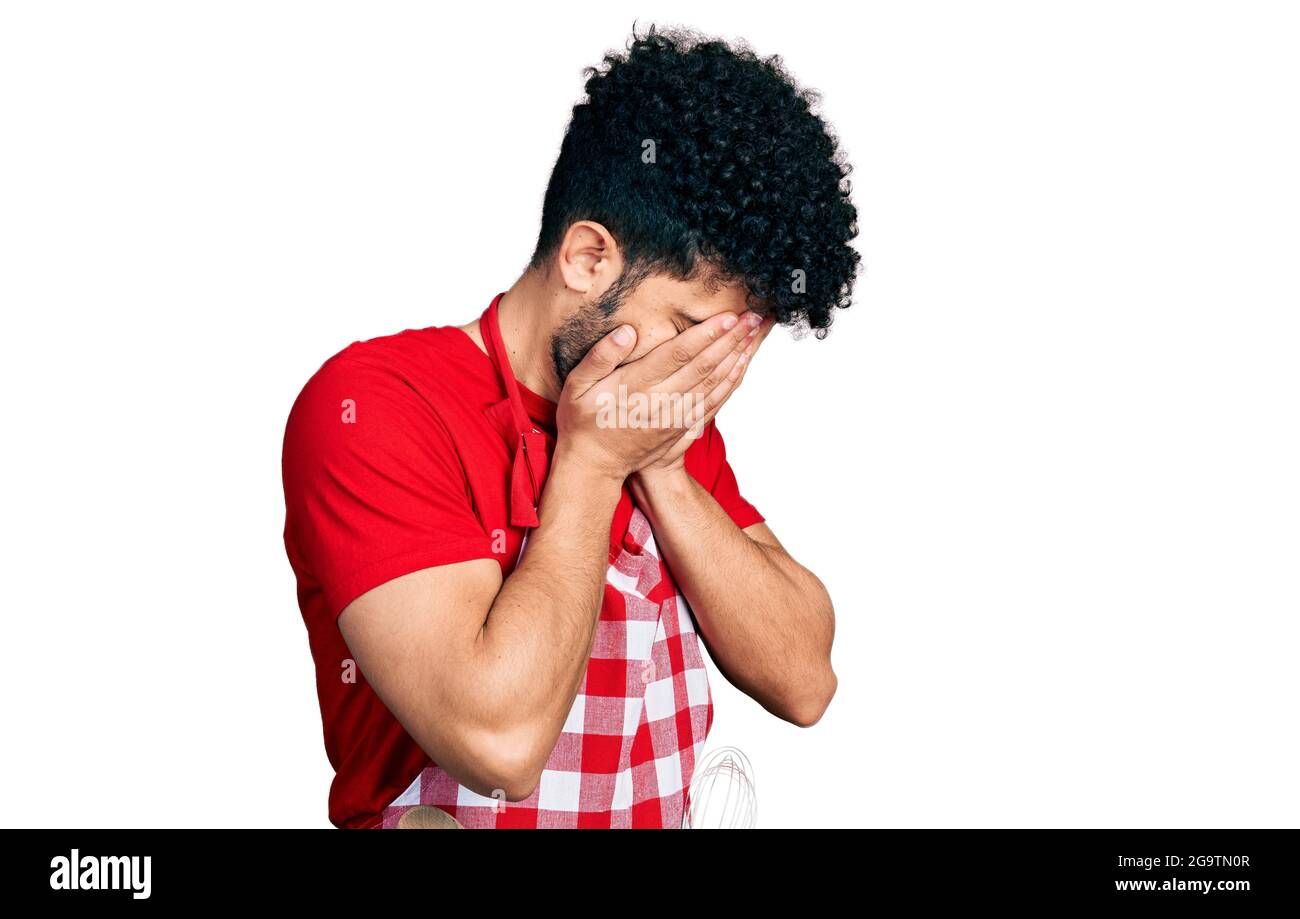 Young arab man with beard wearing cook apron with sad expression ...