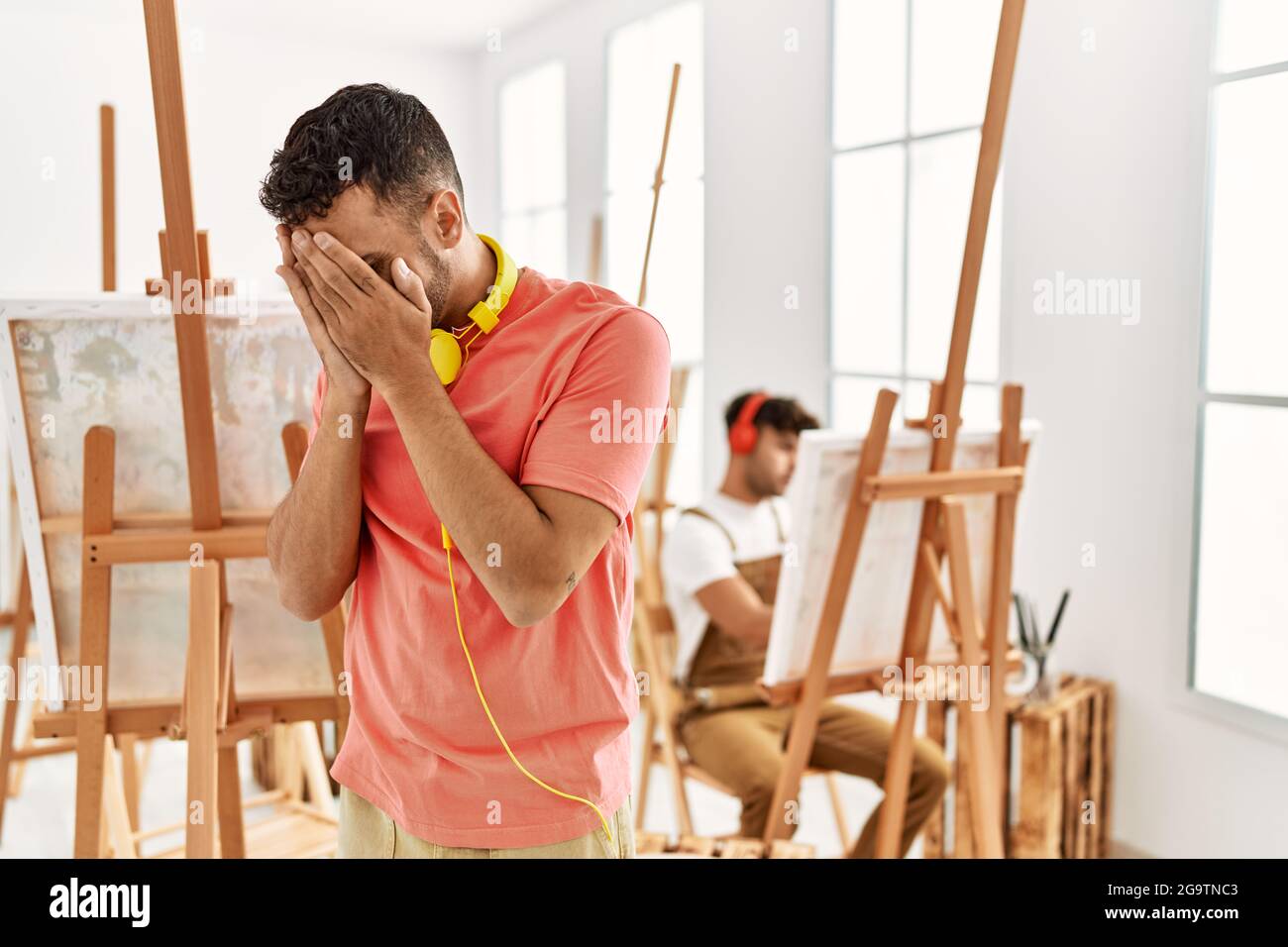 Young hispanic man at art studio with sad expression covering face with ...