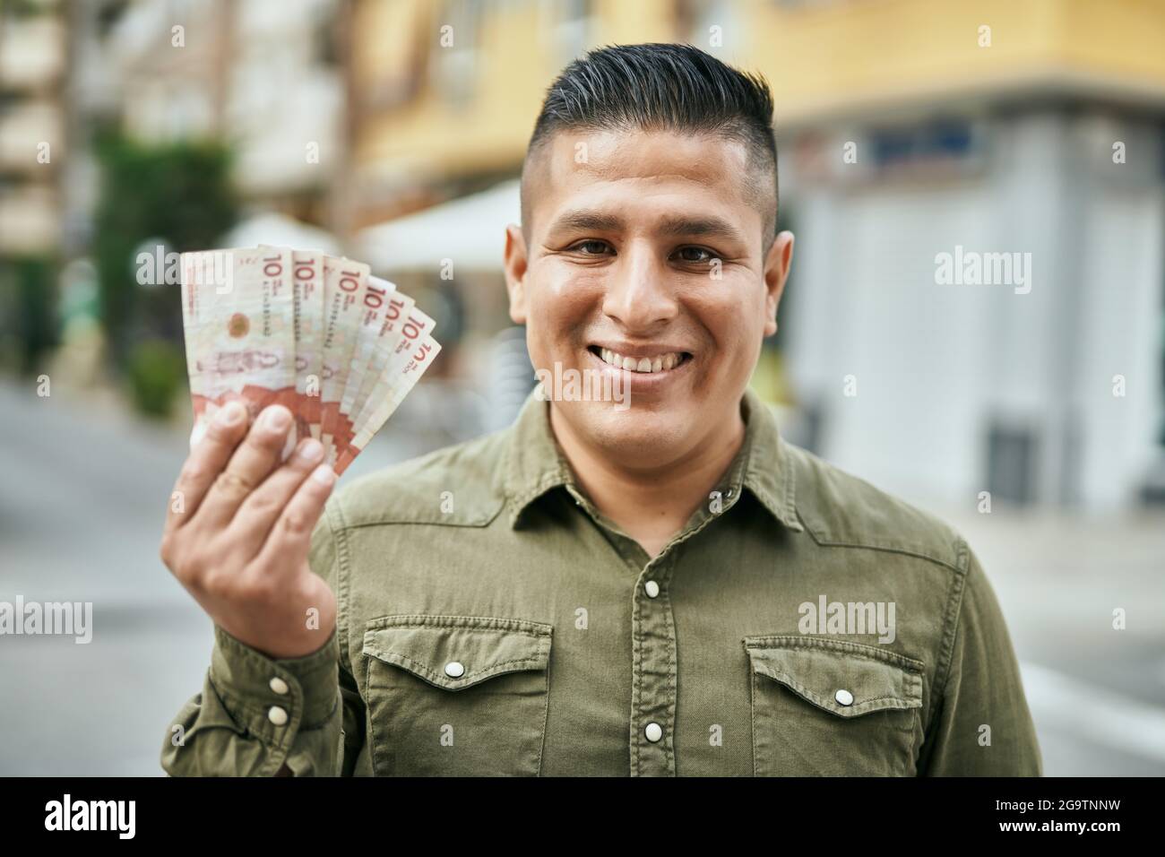 Young latin man smiling happy holding colombian pesos at the city Stock ...