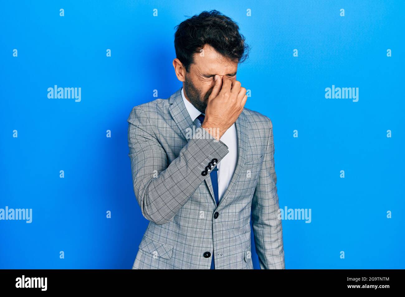 Handsome man with beard wearing business suit and tie tired rubbing ...