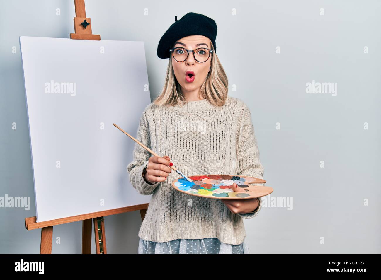 Beautiful caucasian woman drawing with palette on easel stand afraid ...