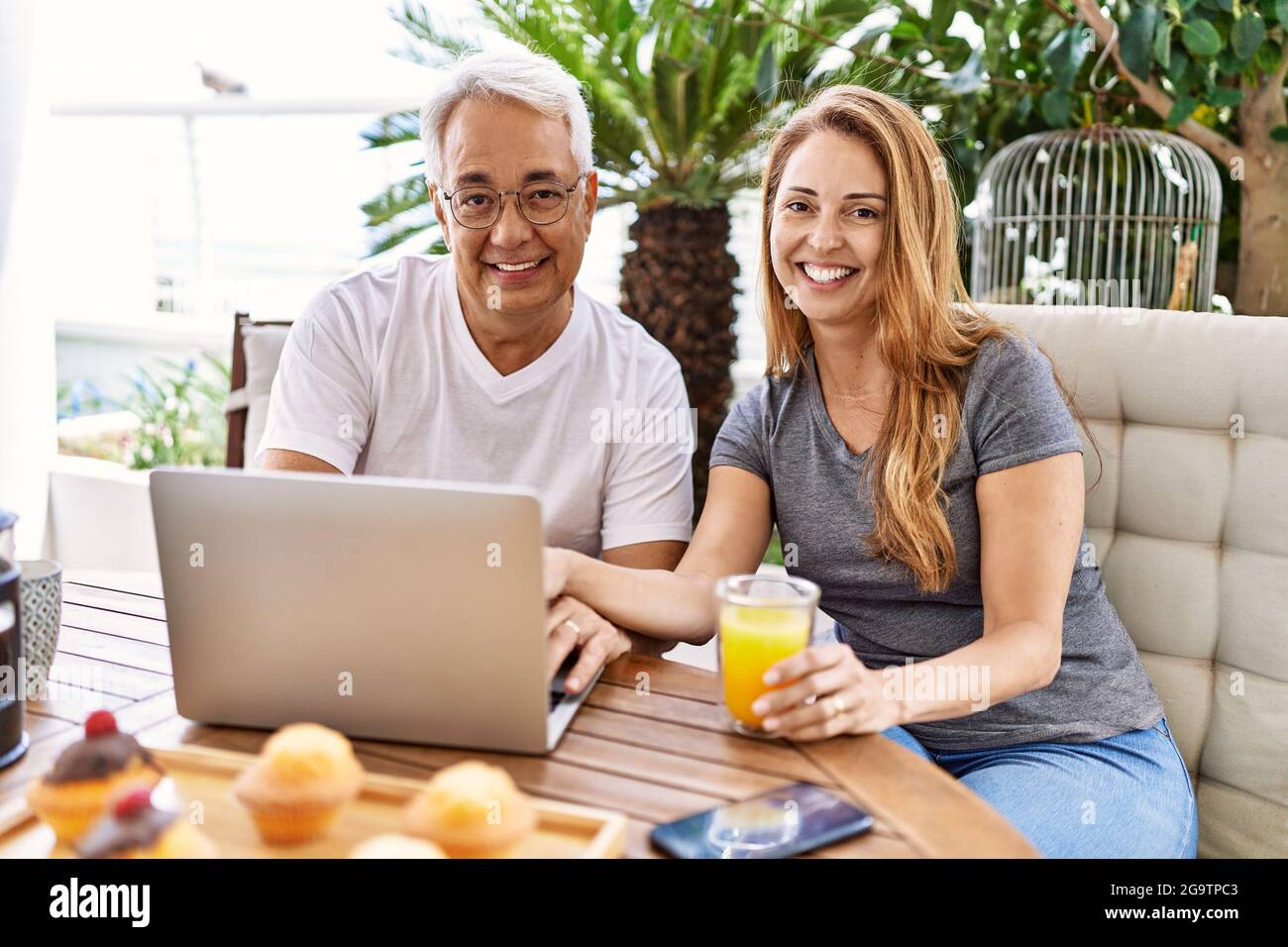 Middle age hispanic couple having breakfast using laptop at the terrace ...