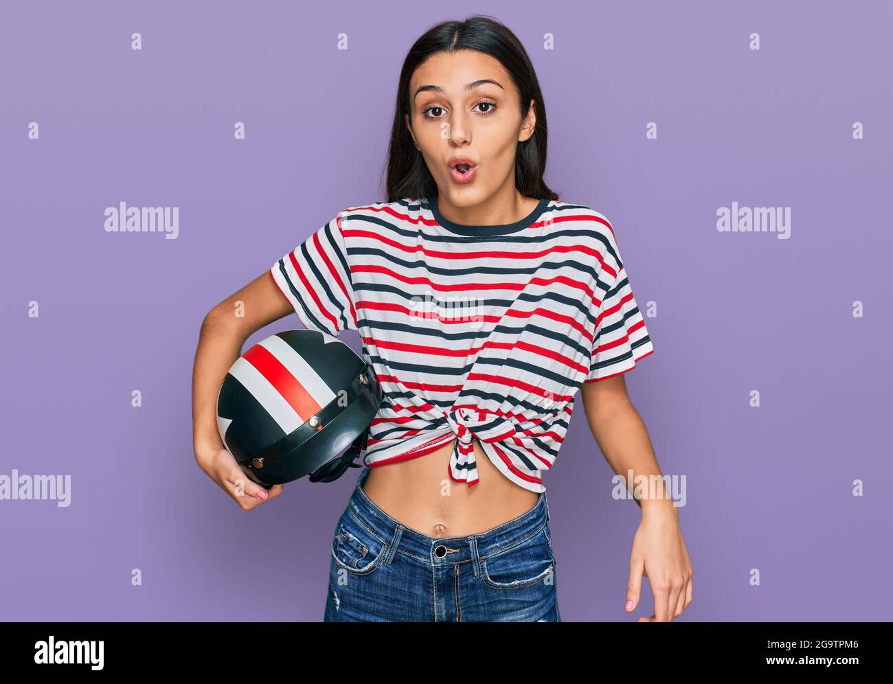 Young hispanic girl holding motorcycle helmet scared and amazed with ...