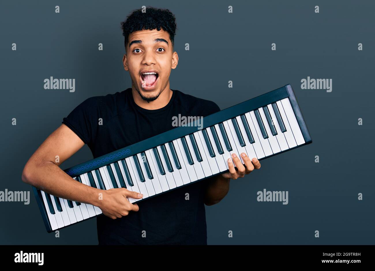 Young african american man holding piano keyboard celebrating crazy and ...