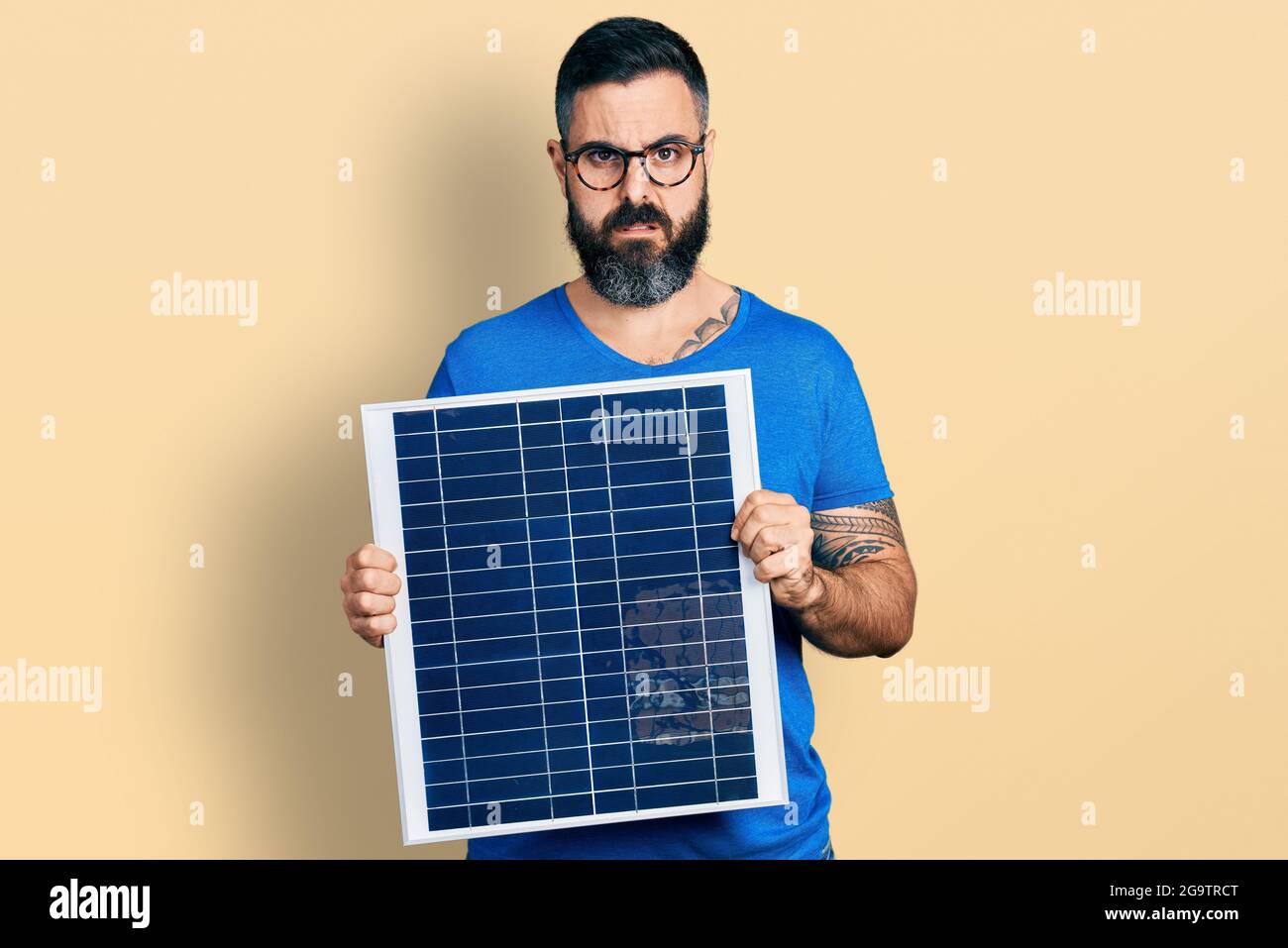 Hispanic man with beard holding photovoltaic solar panel clueless and ...