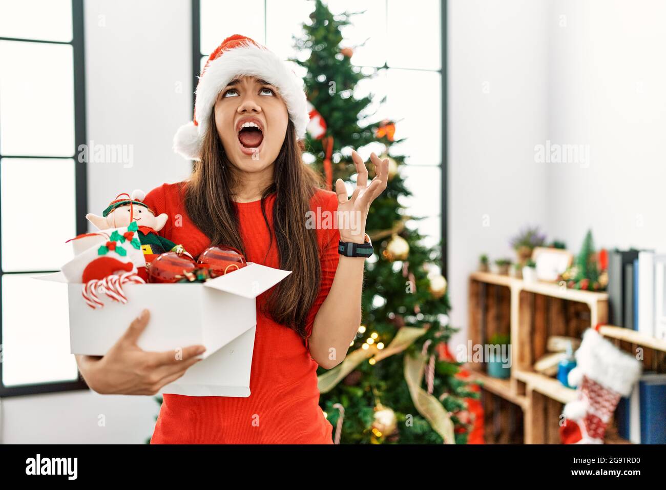 Young brunette woman standing by christmas tree holding decoration ...