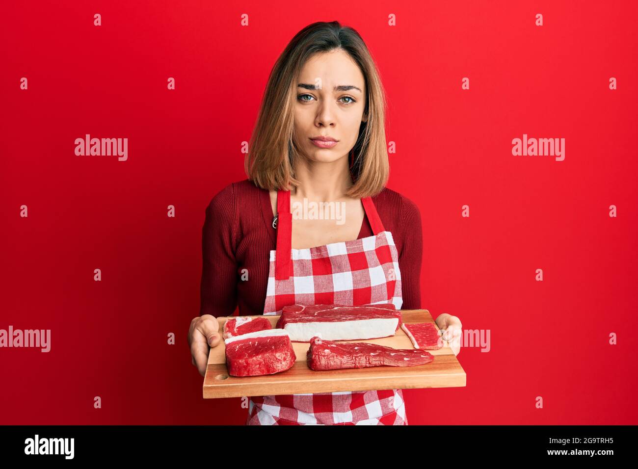 Young caucasian blonde woman holding board with raw meat depressed and ...