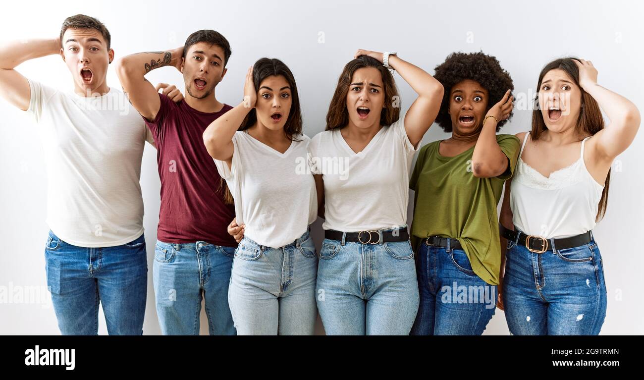 Group of young friends standing together over isolated background crazy and scared with hands on ...