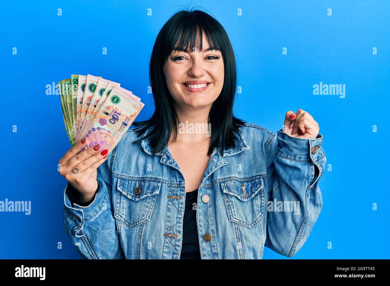 Young hispanic woman holding argentine pesos banknotes screaming proud ...