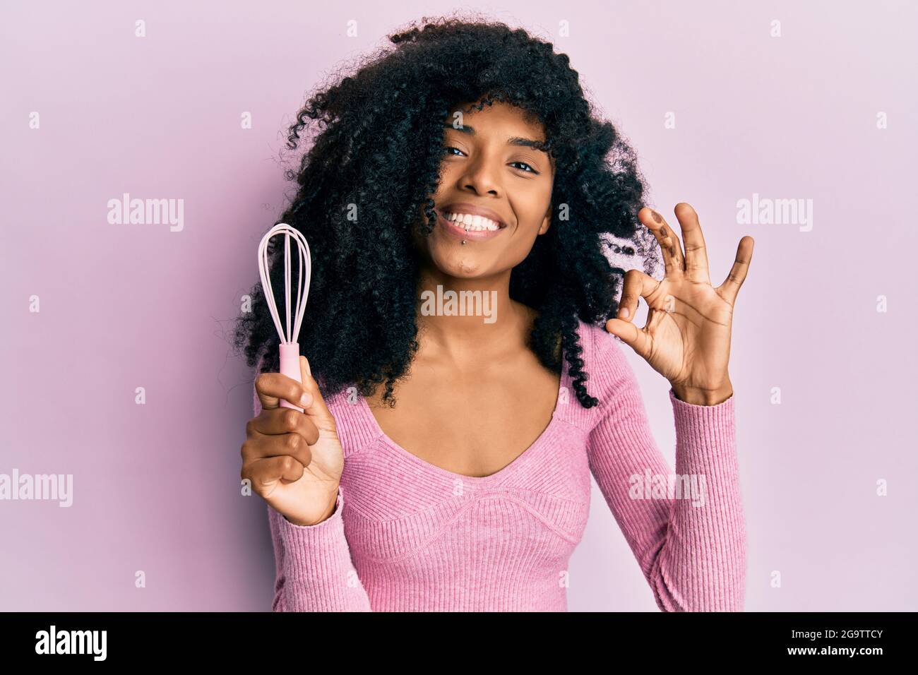 African american woman with afro hair holding small whisk doing ok sign ...