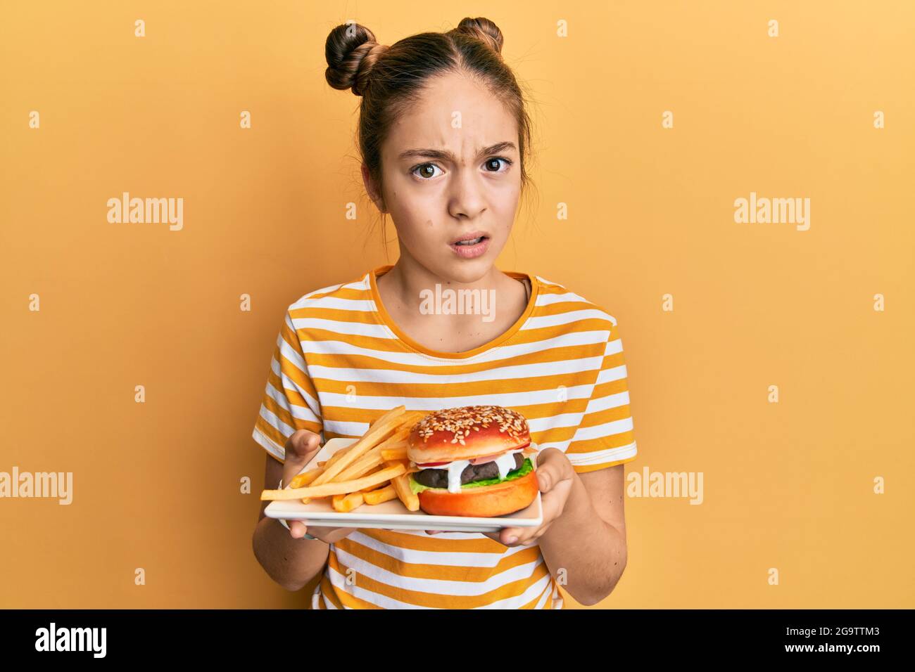 Beautiful brunette little girl eating a tasty classic burger with fries ...