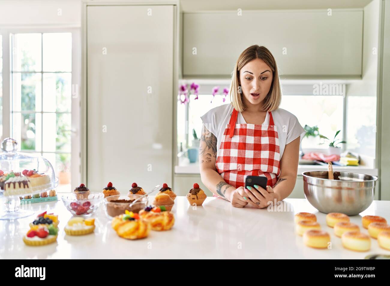Young beautiful blonde woman wearing apron cooking pastries looking for ...