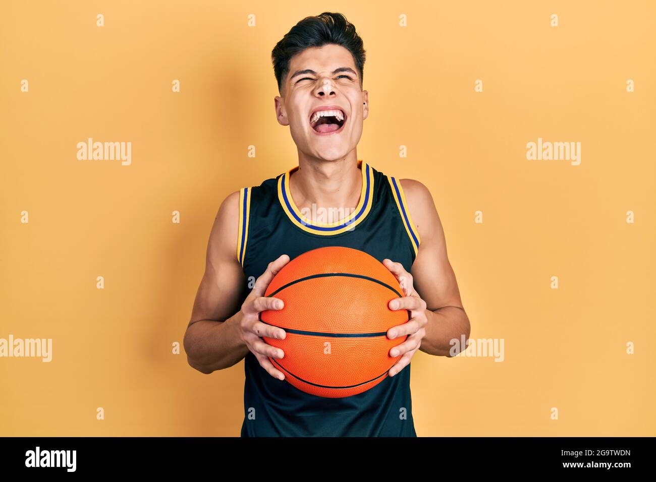 Young hispanic man holding basketball ball angry and mad screaming ...