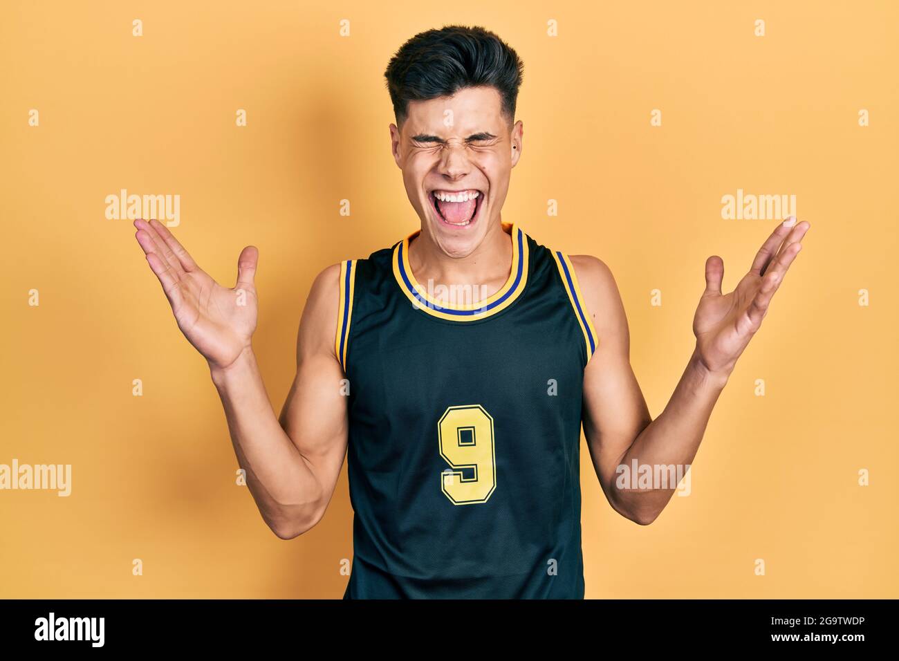 Young hispanic man wearing basketball uniform celebrating mad and crazy ...