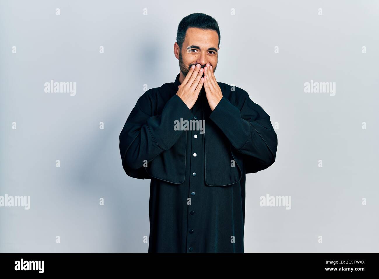 Handsome hispanic man with beard wearing catholic priest robe laughing ...