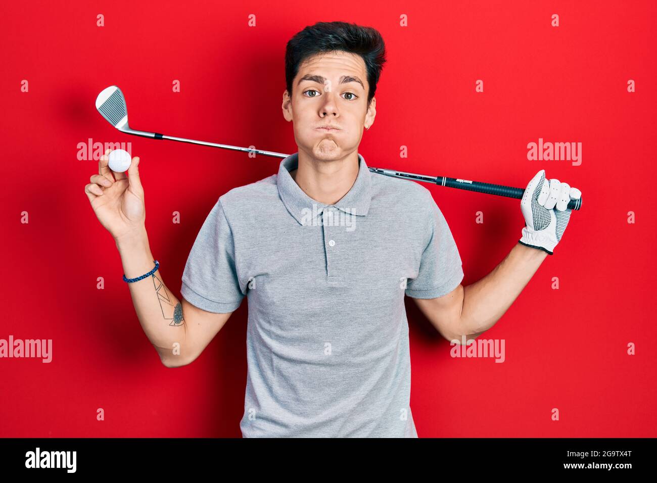 Young hispanic man holding golf ball puffing cheeks with funny face ...