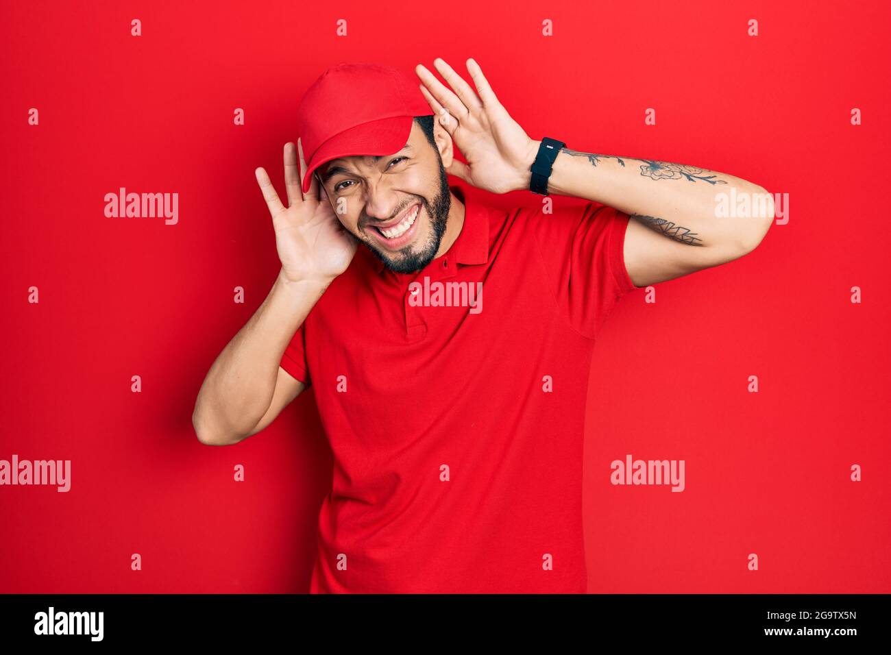 Hispanic man with beard wearing delivery uniform and cap trying to hear ...