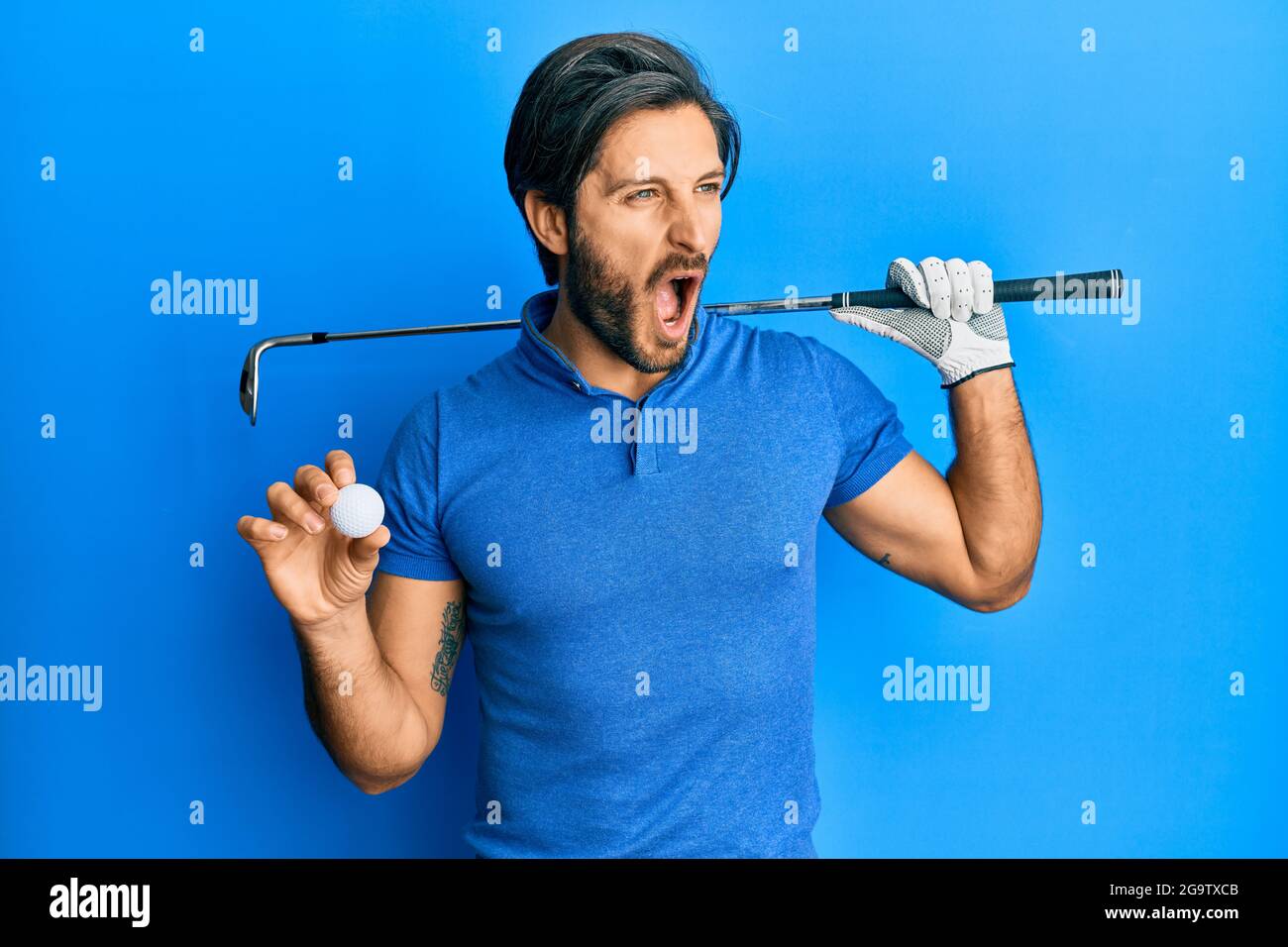 Young hispanic man holding golf ball angry and mad screaming frustrated ...