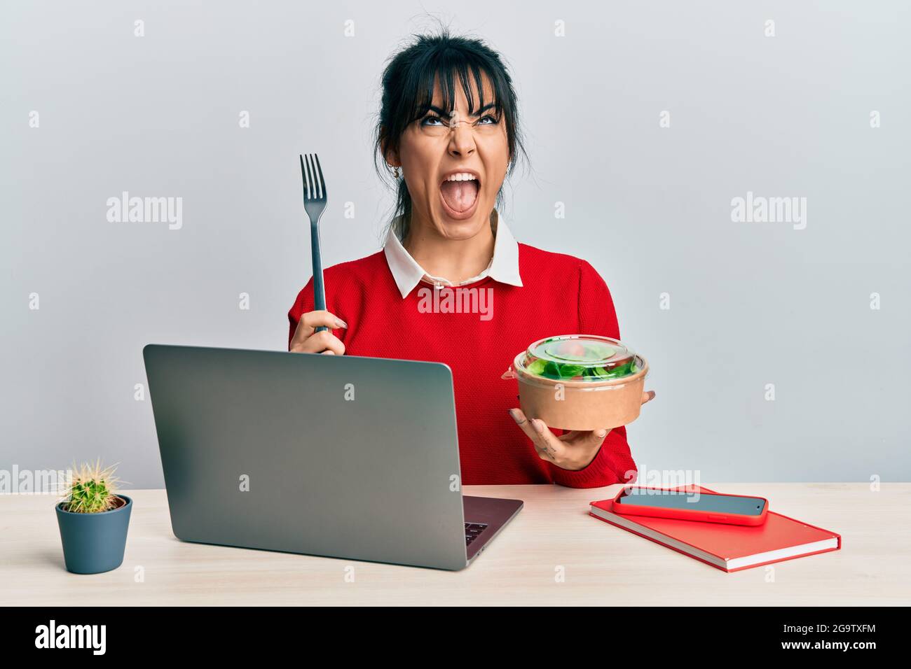 Young brunette woman with bangs working at the office eating healthy ...