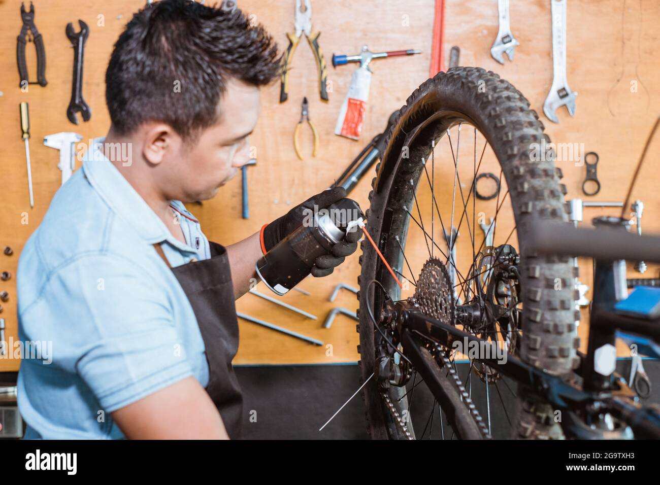 a young mechanic wearing gloves using chain lube lubricating the chain ...