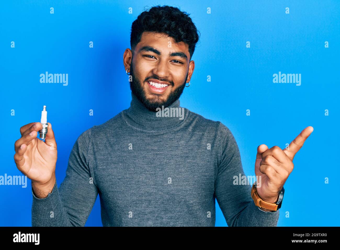 Arab man with beard holding spark plug smiling happy pointing with hand ...
