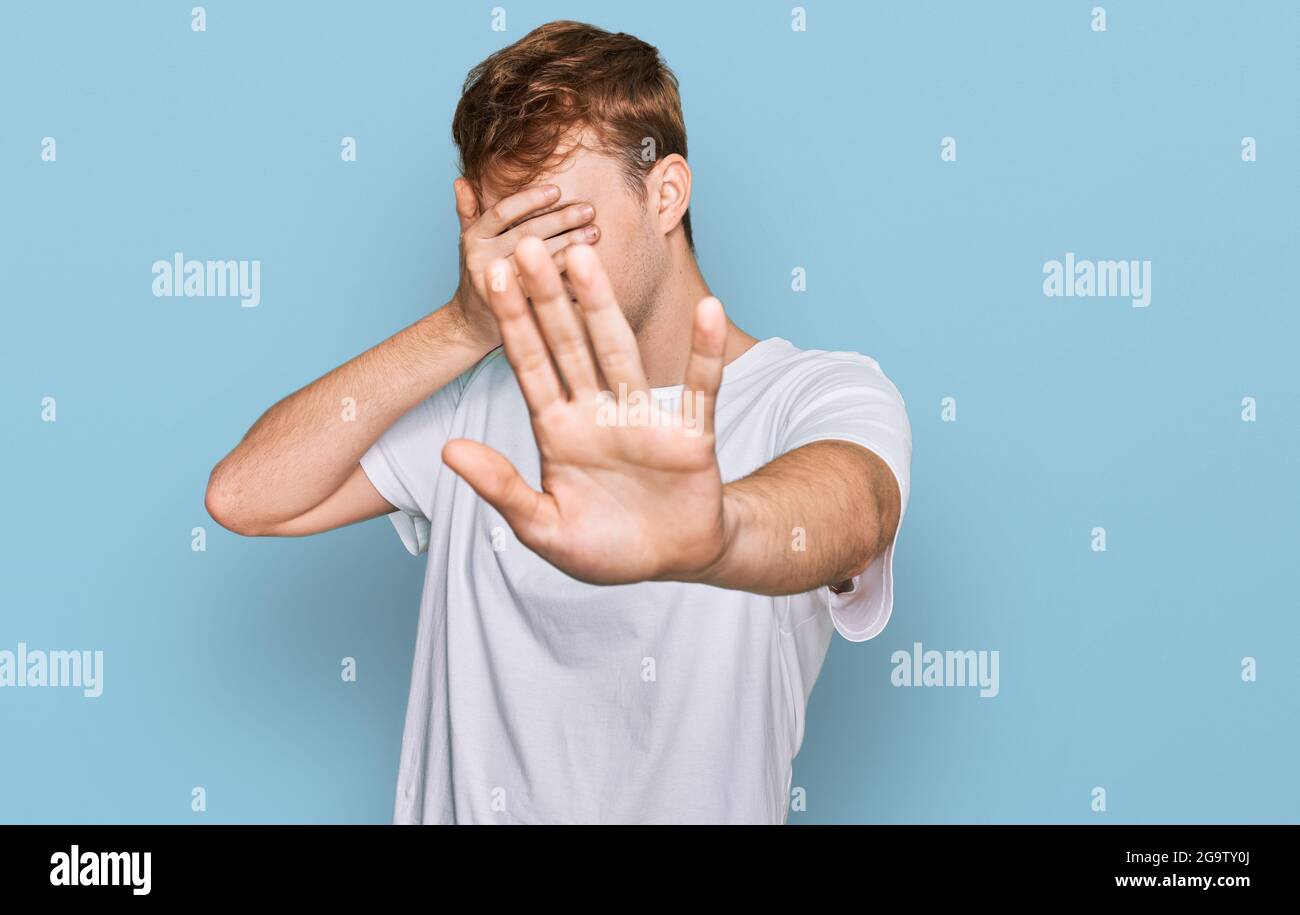 Young caucasian man wearing casual white t shirt covering eyes with ...