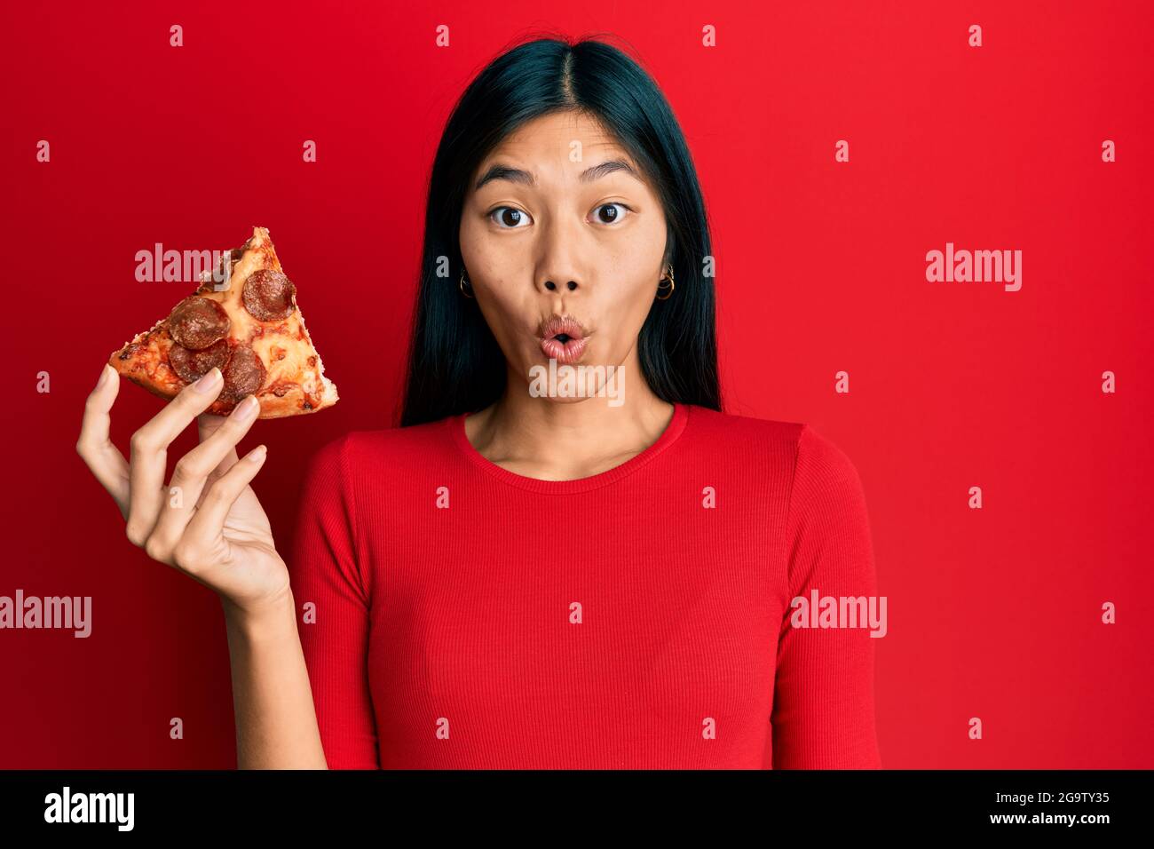Young chinese woman holding italian pizza scared and amazed with open ...