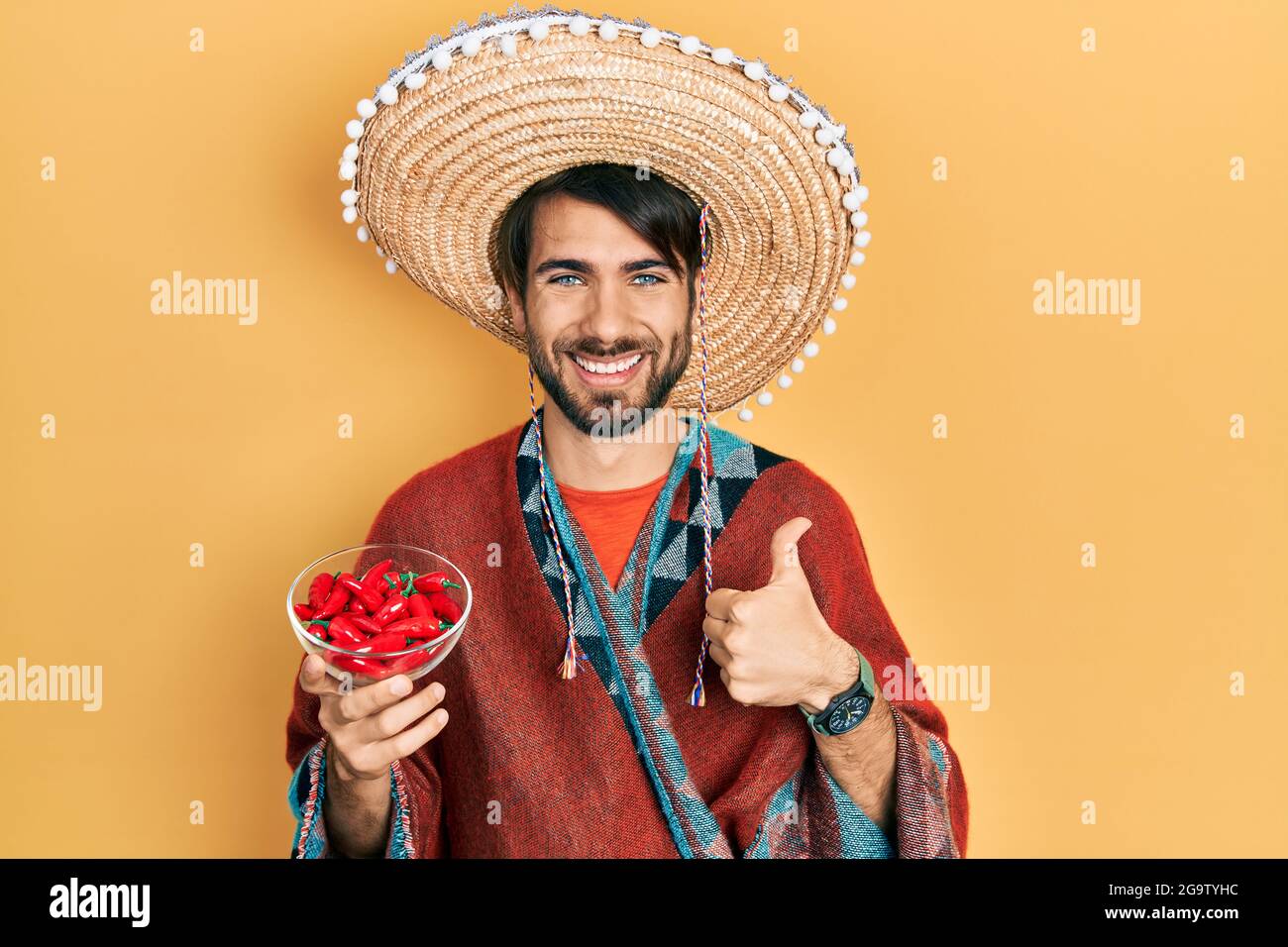 Young hispanic man wearing mexican hat holding chili smiling happy and ...