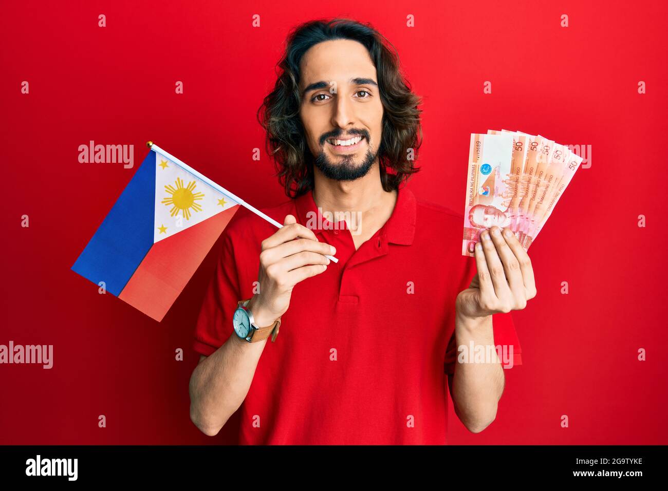 Young hispanic man holding philippines flag and pesos banknotes smiling ...