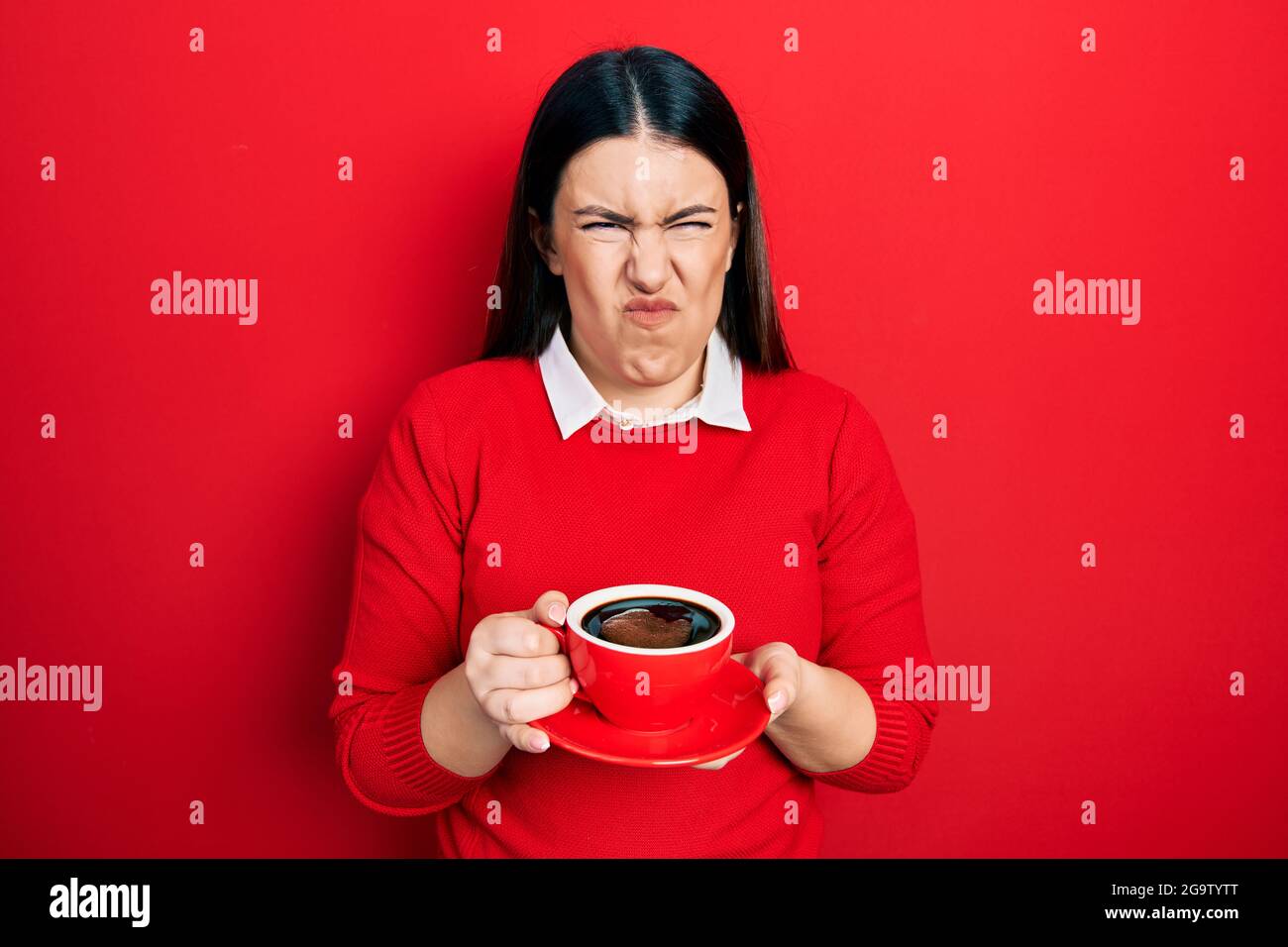 Young hispanic woman drinking a cup of coffee skeptic and nervous ...
