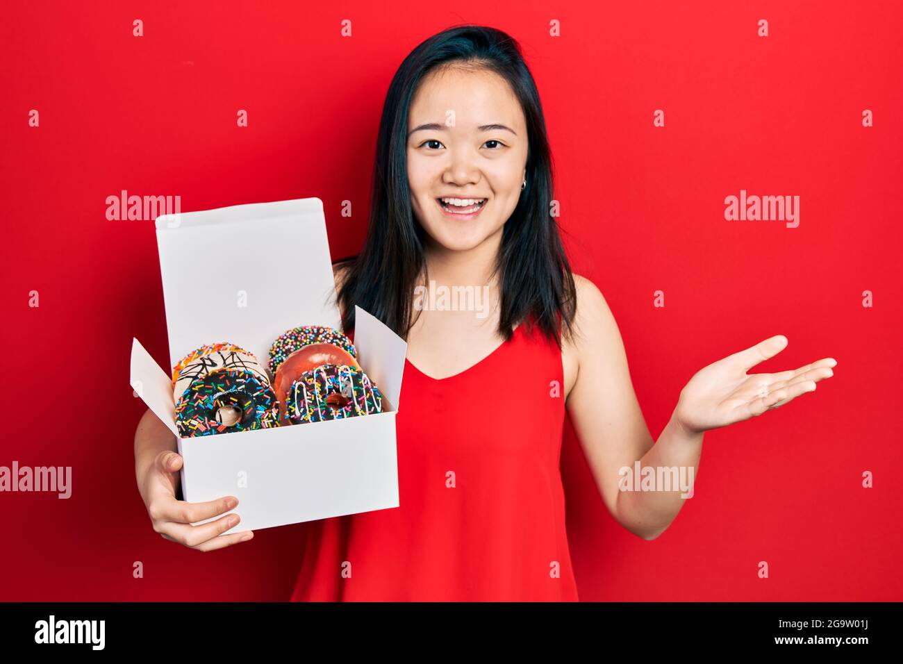 Young chinese girl holding box with tasty colorful doughnuts ...